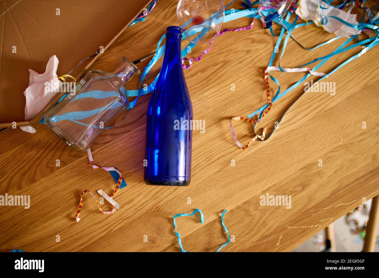 Messy wooden table with pizza box, empty blue bottles, wine glass and ...