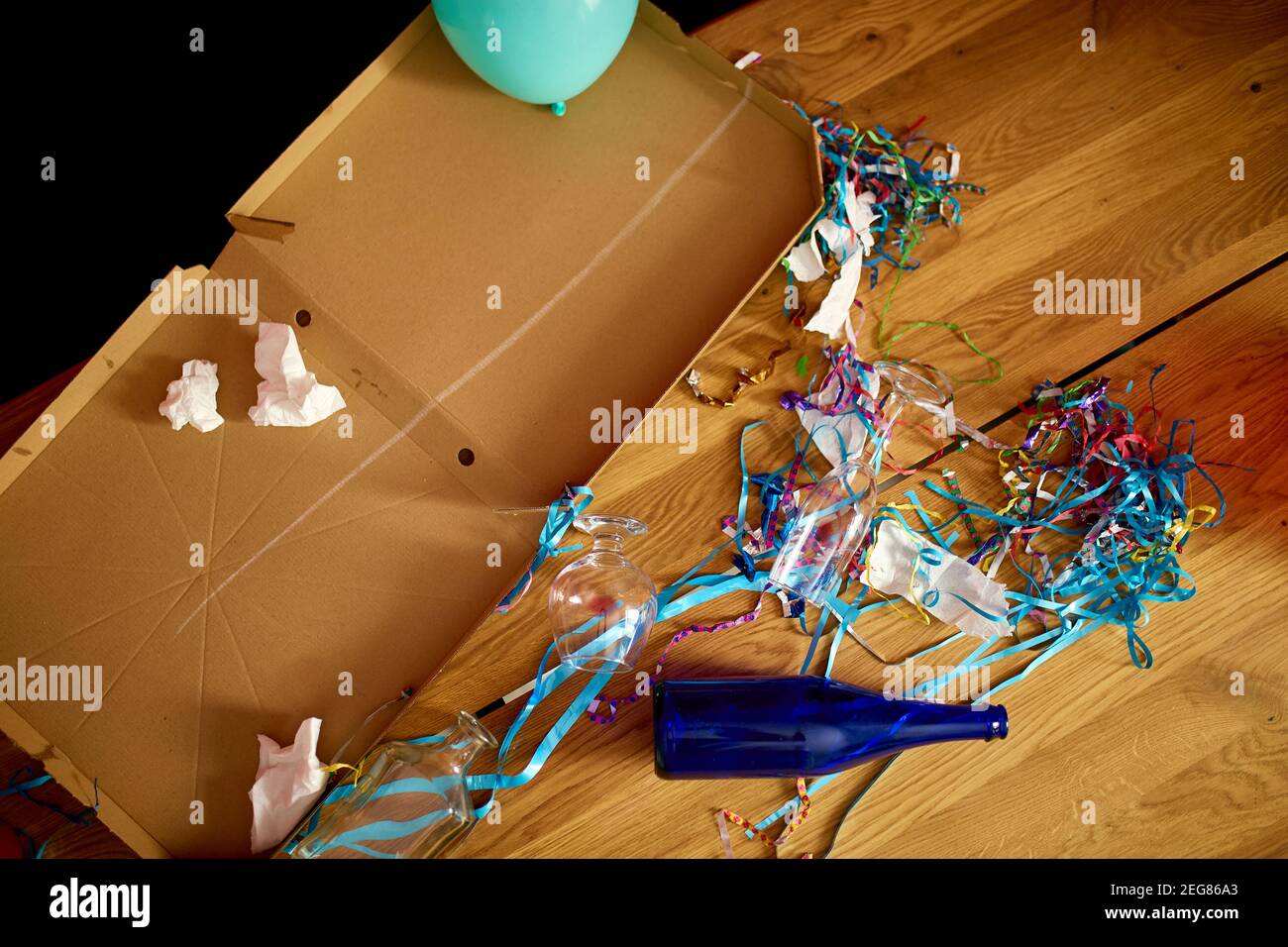 Messy wooden table with pizza box, empty blue bottles, wine glass and ...