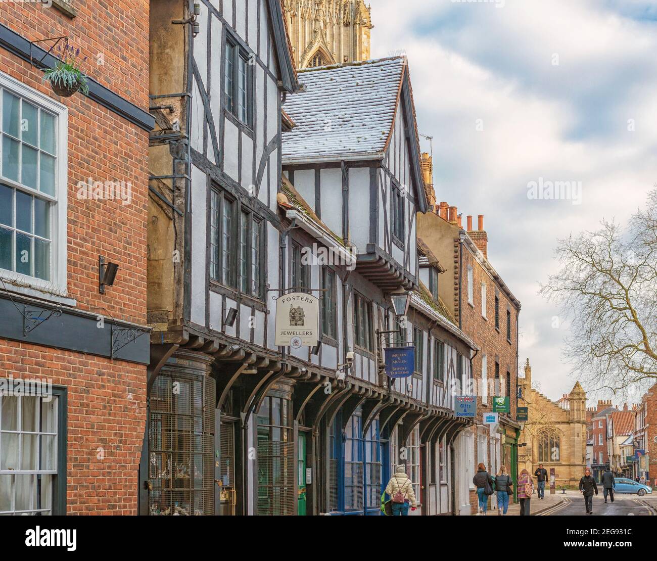 An old half-timbered building with snow on the roof. There are shops on ...