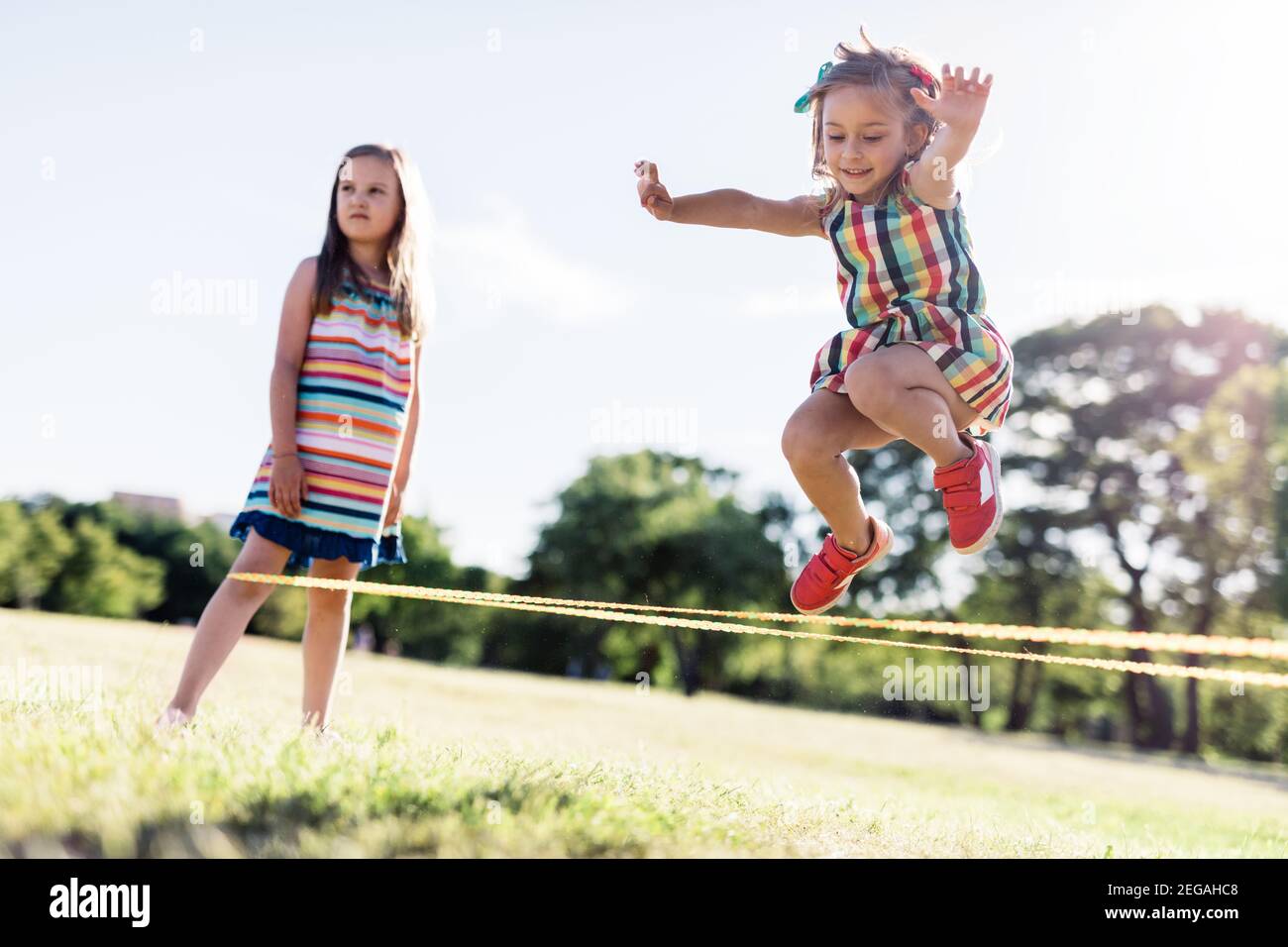 Little girl in a colorful dress jumping through the elastic. Childhood game. Chinese jumping ...
