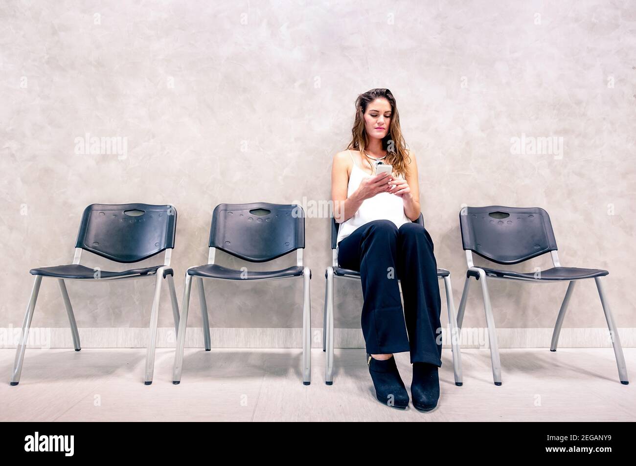 Pensive young woman with mobile smart phone sitting in waiting room ...