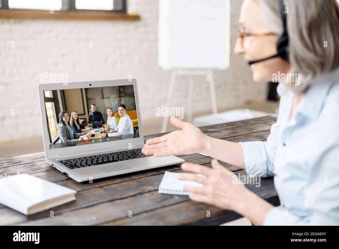 Group of people on the laptop screen, a mature coach wearing headset ...