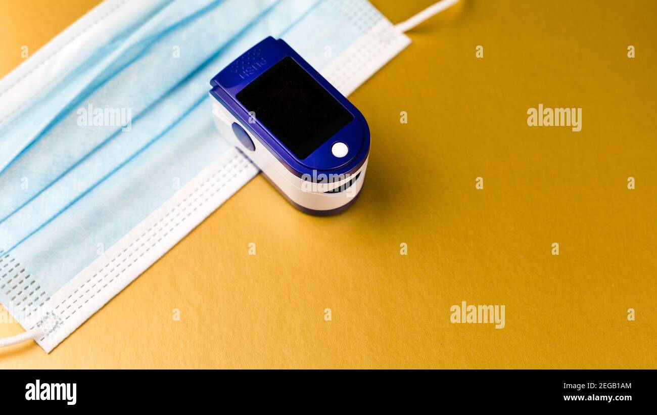Oximeter and protective medical mask on a gold background. Copy space ...