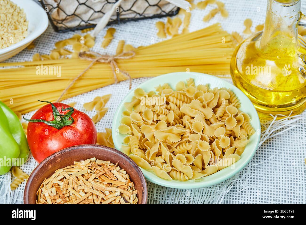 Bowls of uncooked pasta, spaghetti, vegetables, and a bottle of oil ...