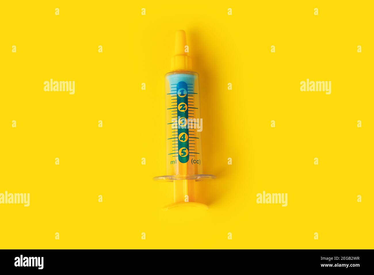 A plastic miniature toy syringe over yellow background, medicine and ...