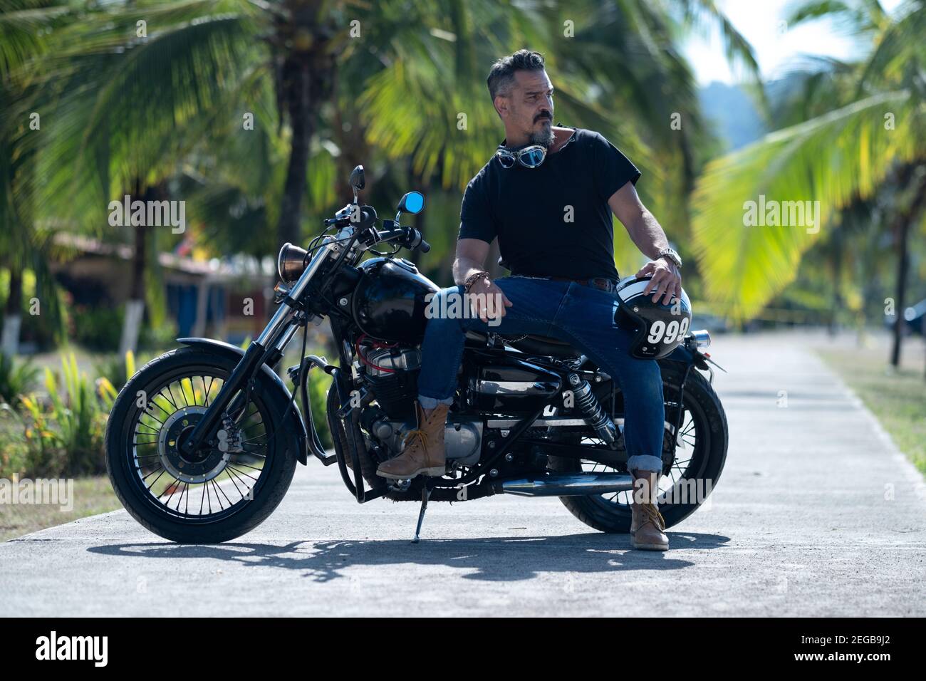 Male biker with a thick beard poses on a motorbike in a beautiful park ...