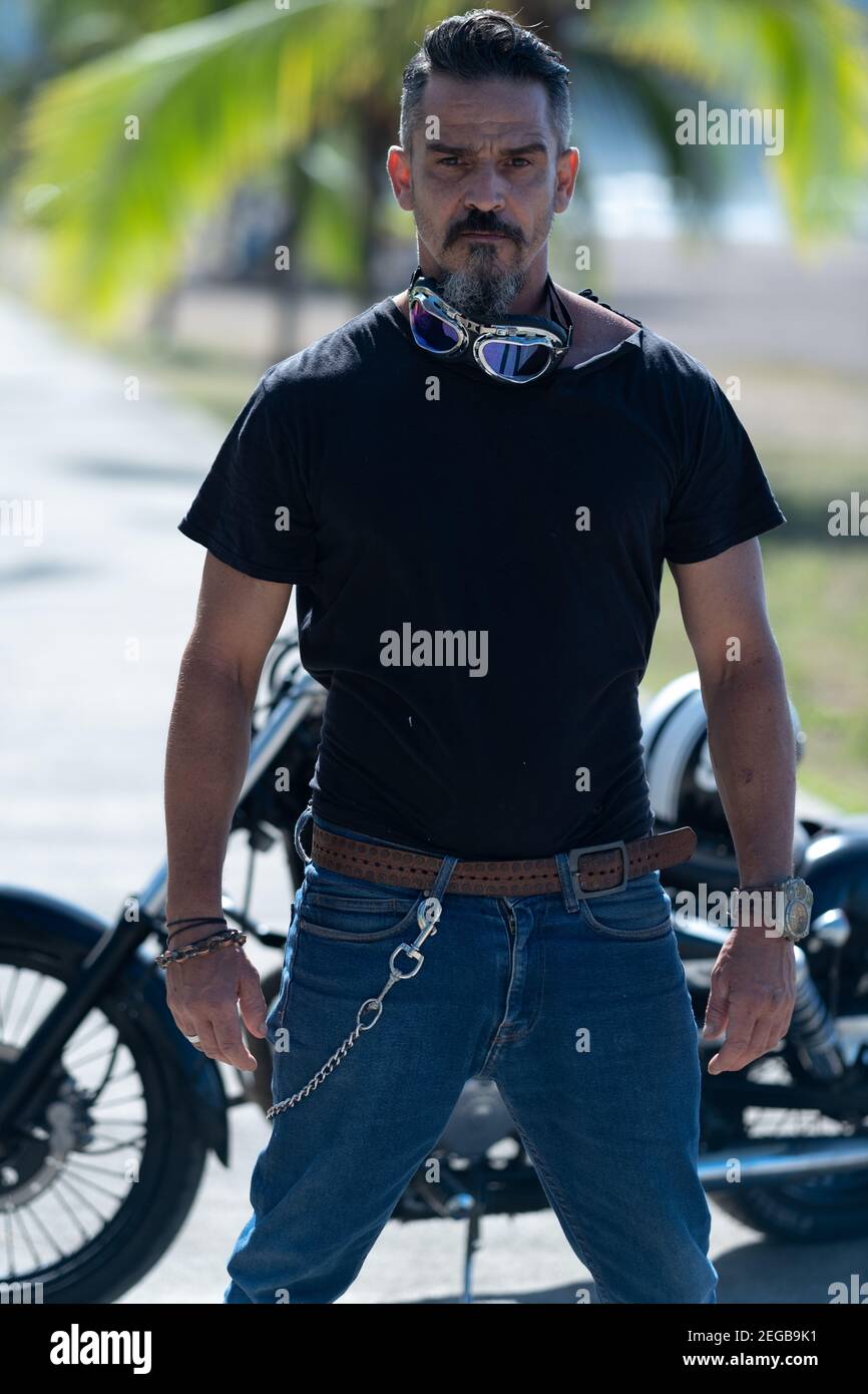 Male biker with a thick beard poses on a motorbike in a beautiful park ...