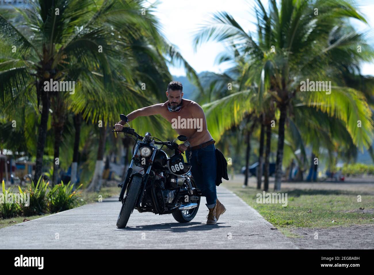 Male biker with a thick beard poses on a motorbike in a beautiful park ...