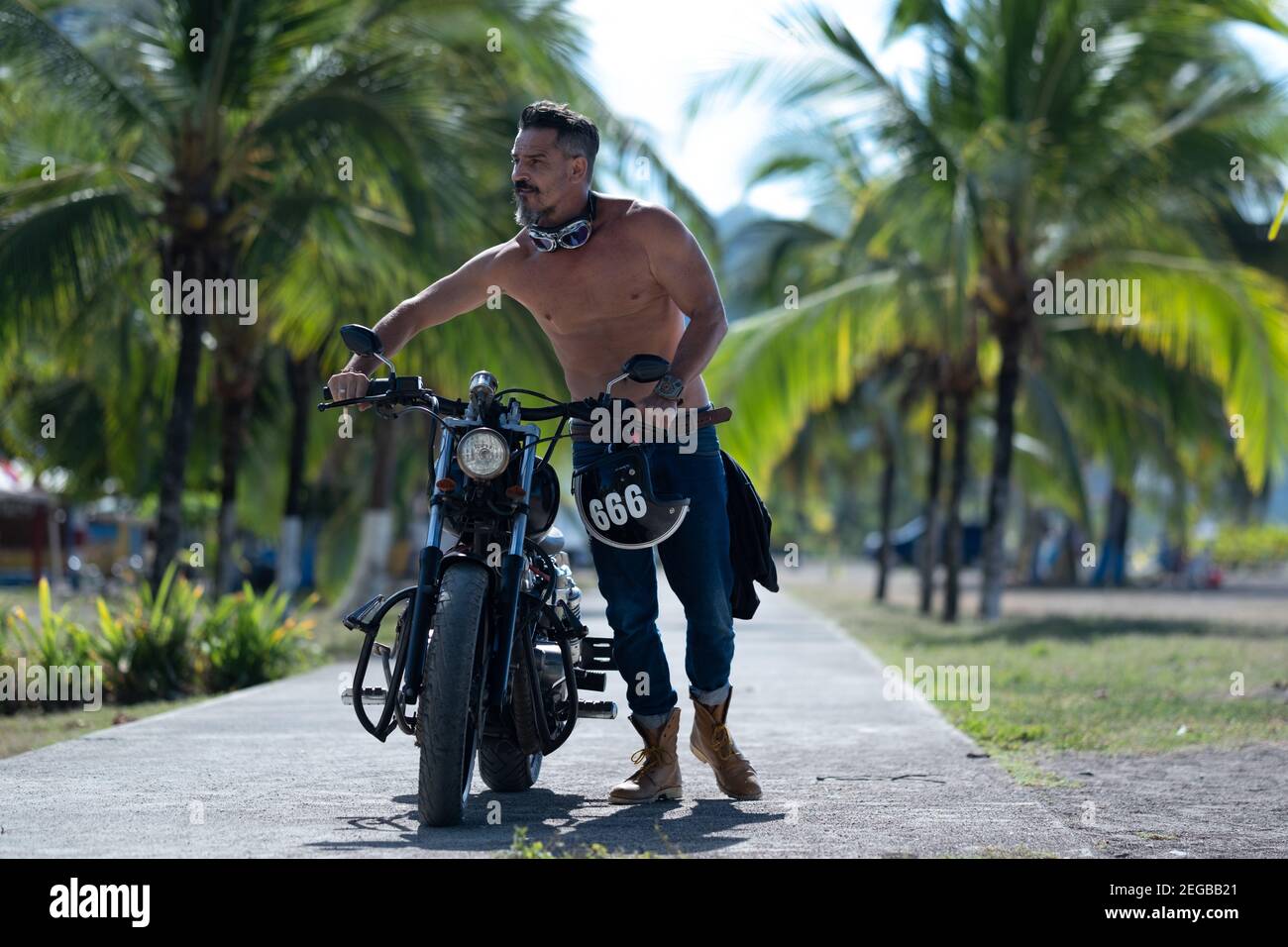 Male biker with a thick beard poses on a motorbike in a beautiful park ...