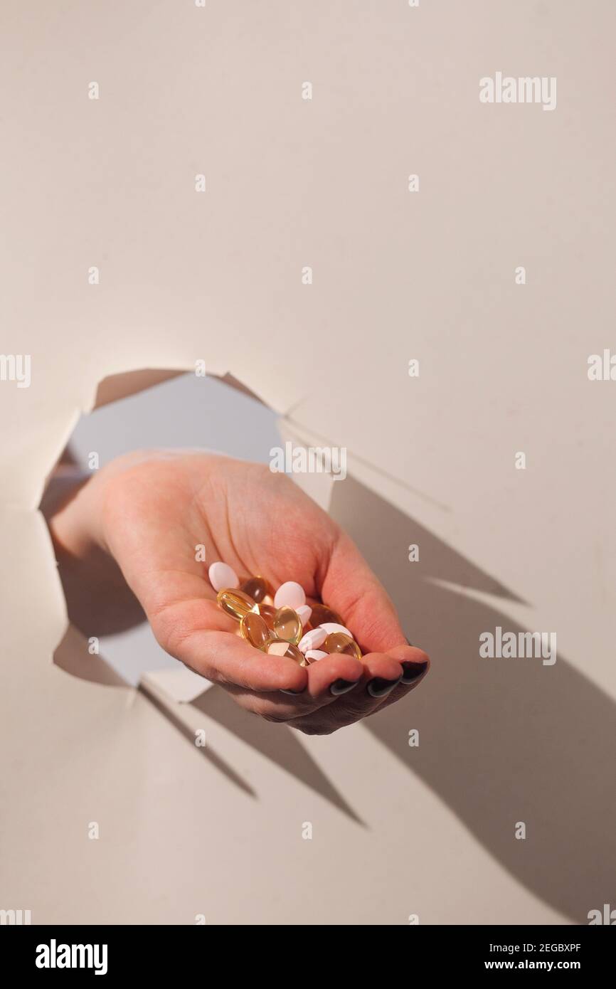 A handful of tablets and pills in hand. The hand breaks through a hole ...