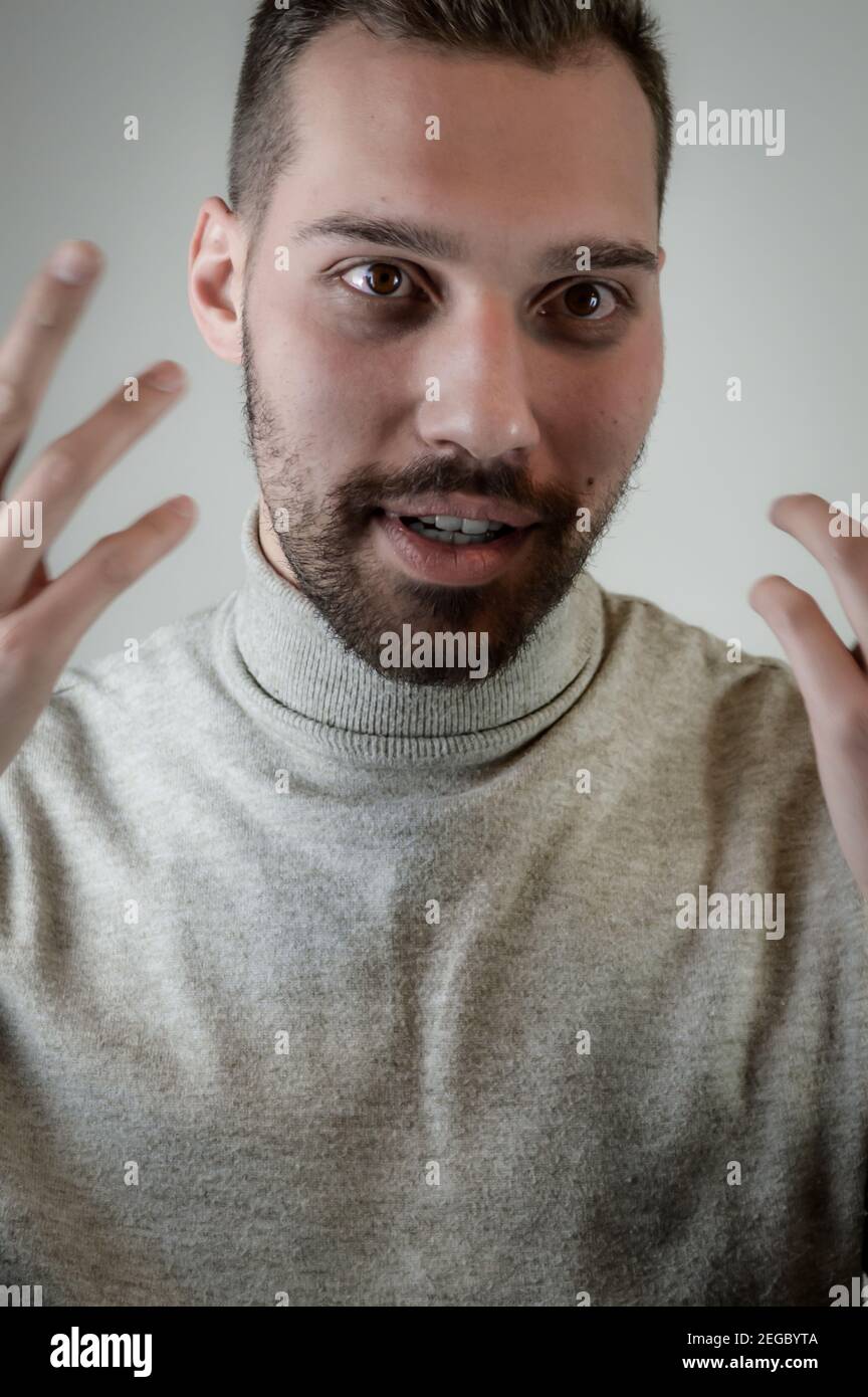Young man with a short beard speaks gesturing with his hands to explain ...
