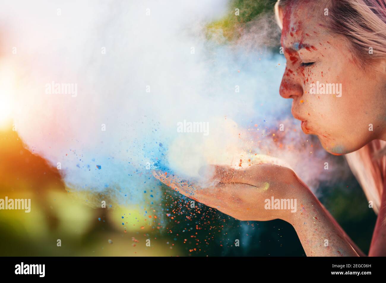 Woman blowing colorful holi powder, creating colorful cloud of dust ...