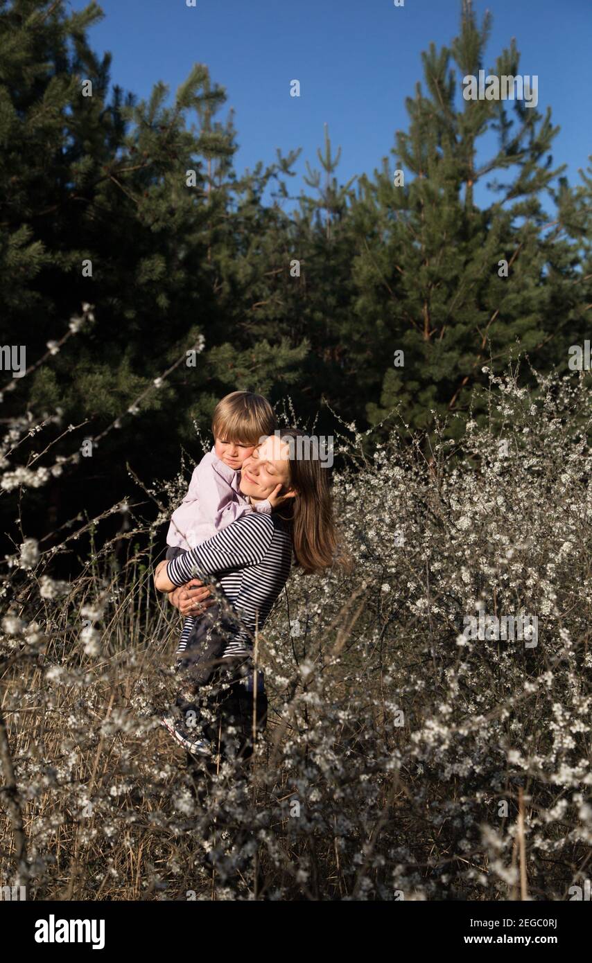 Happy mom and cute son hug among the white flowering trees in the ...