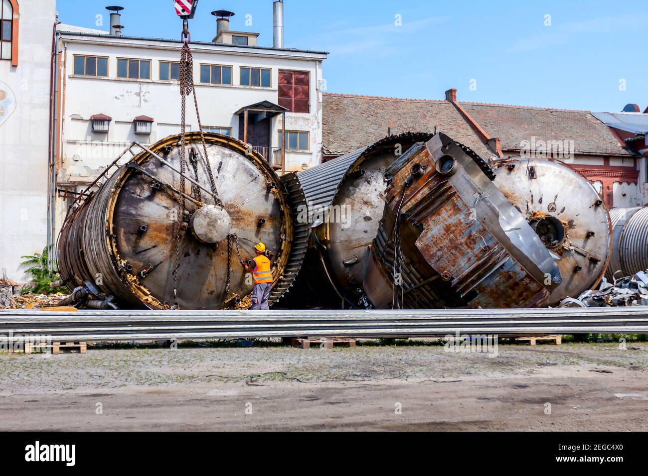 Crane is bringing down heavy metal silo in industrial complex. Worker ...