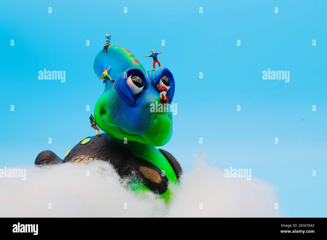 Model climbers on a blue and green dragon with its head in the clouds ...