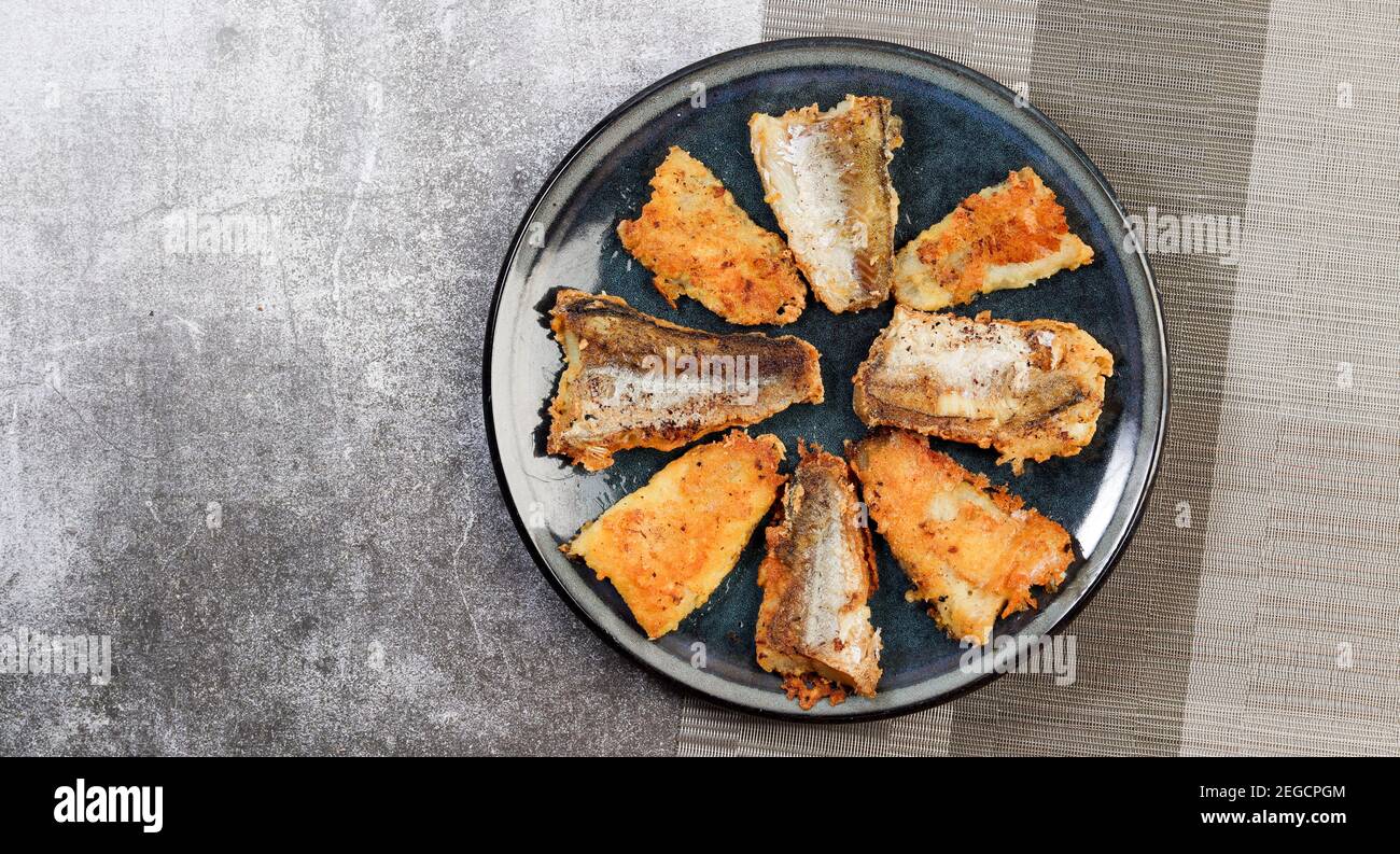 Fried Pollock (hake) fish fillet on a round plate on a dark gray ...