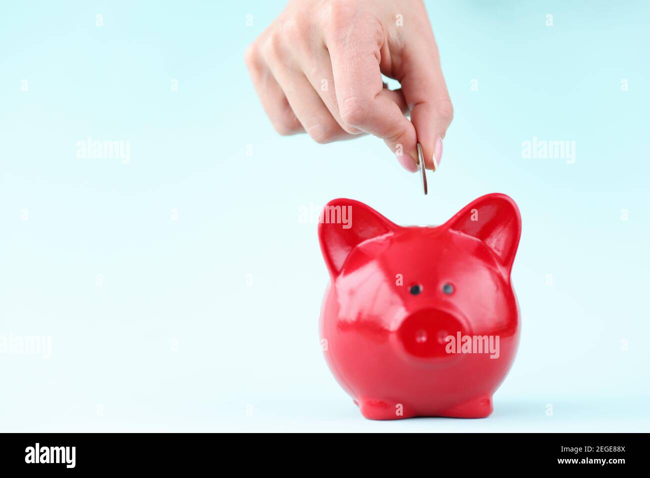Womans hand throwing coin into red piggy bank closeup Stock Photo - Alamy