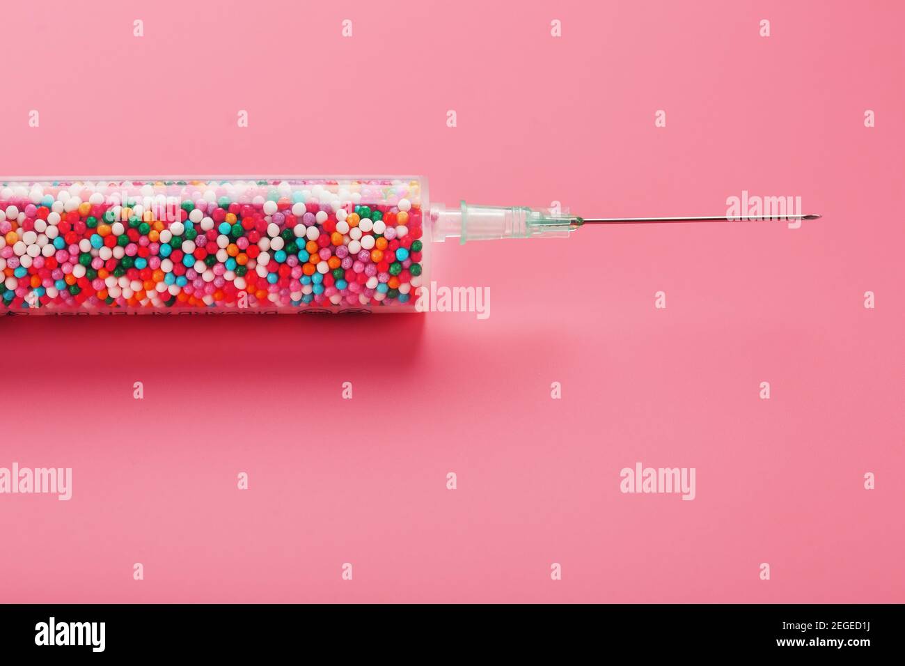 Medical Syringe filled with colorful balloons on a pink background with ...