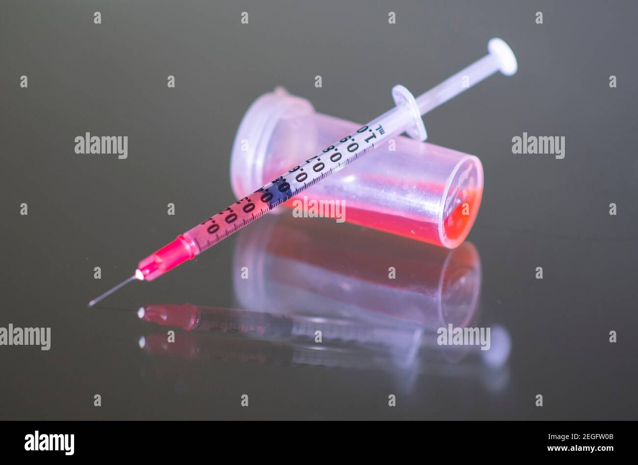 A syringe and a vial containing red fluid is shown on a glass table ...