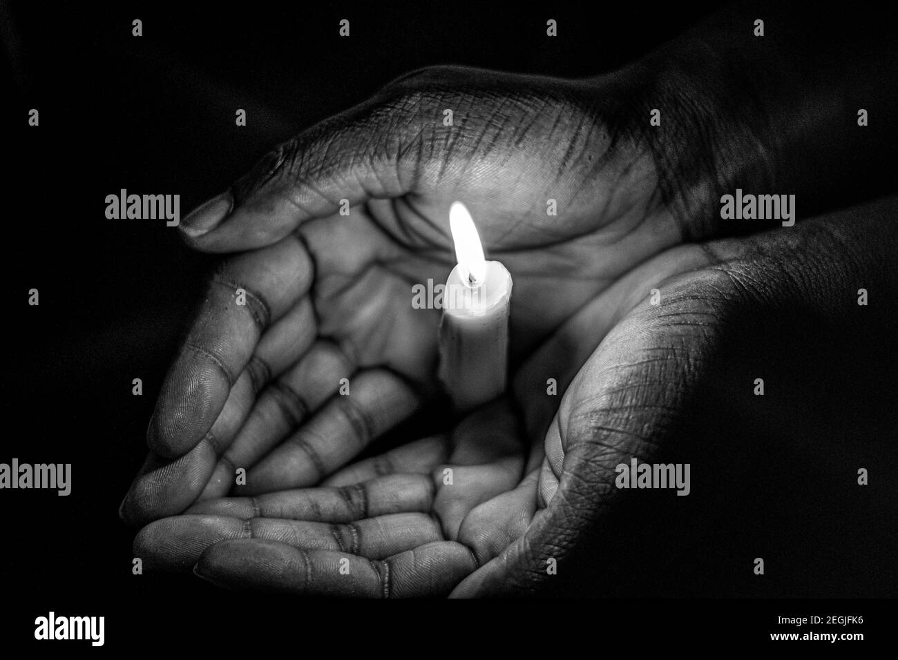 Grayscale closeup of hand palms with a lit candle inside in a darkness ...