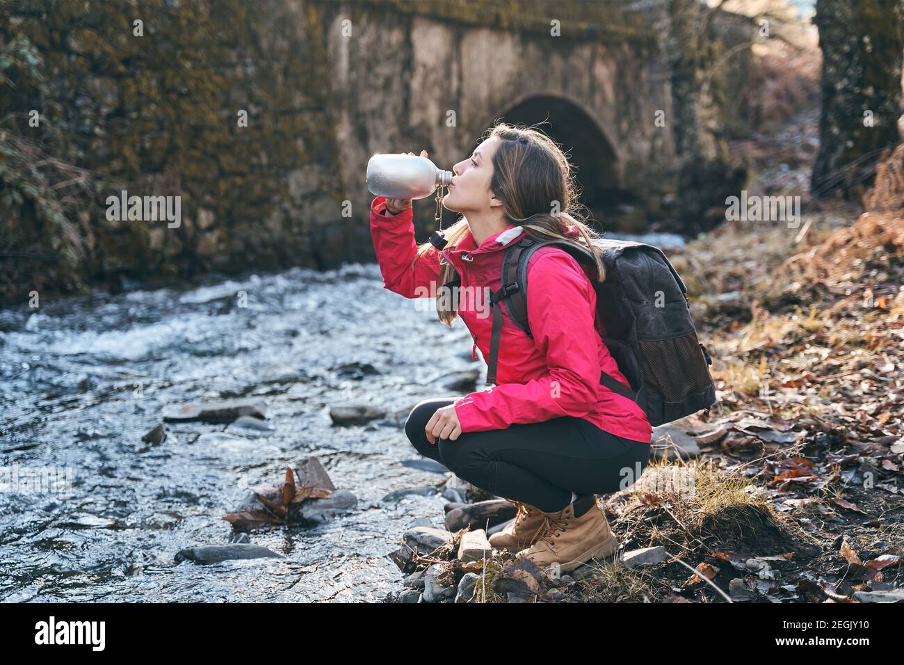 Young woman drinking water from the stream outdoors with a canteen ...