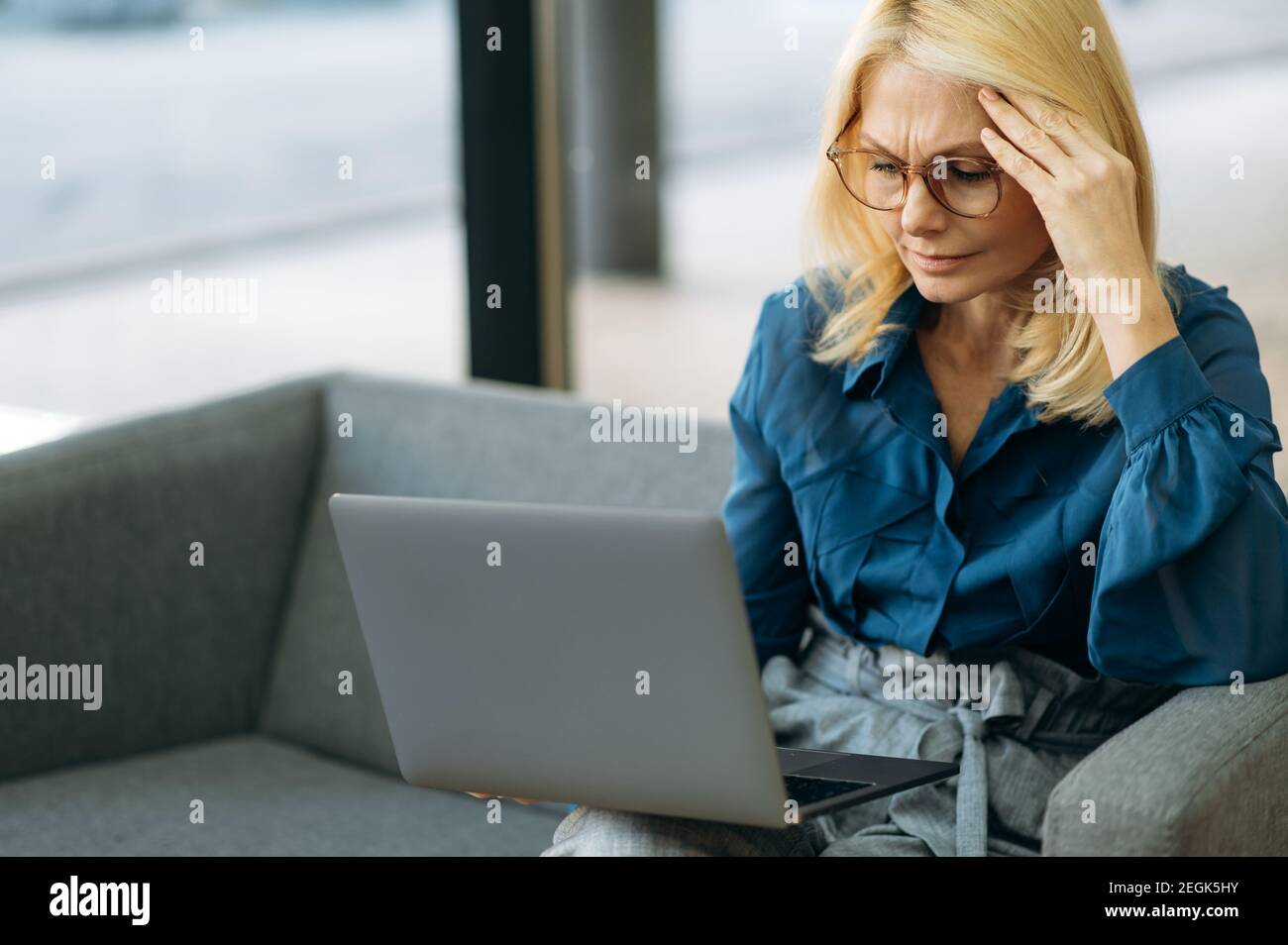 Mature elegant woman in eyeglasses sit on the sofa, having a headache ...