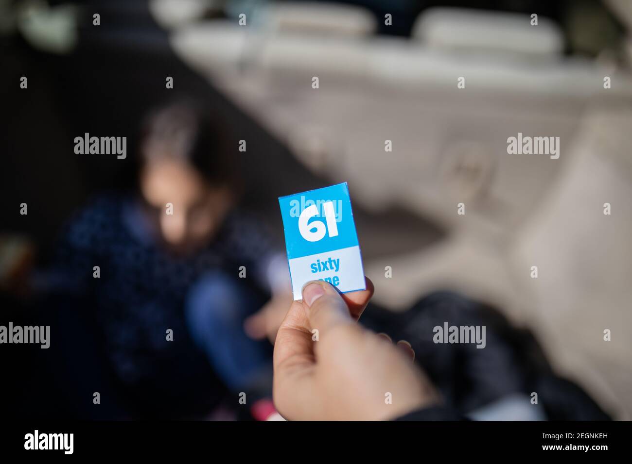 Female hand holding a card with the number 61 with blurry background ...