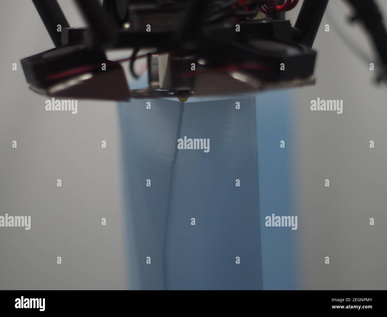 Closeup of 3D printer tip as it extrude plastic layers, blue ...