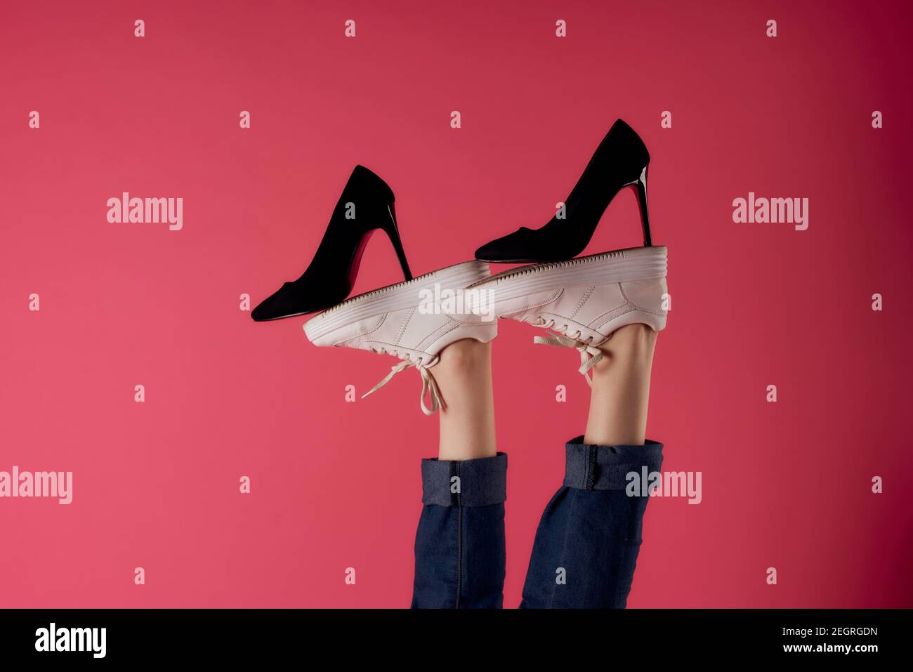 Inverted female legs in white sneakers black shoes top pink background ...
