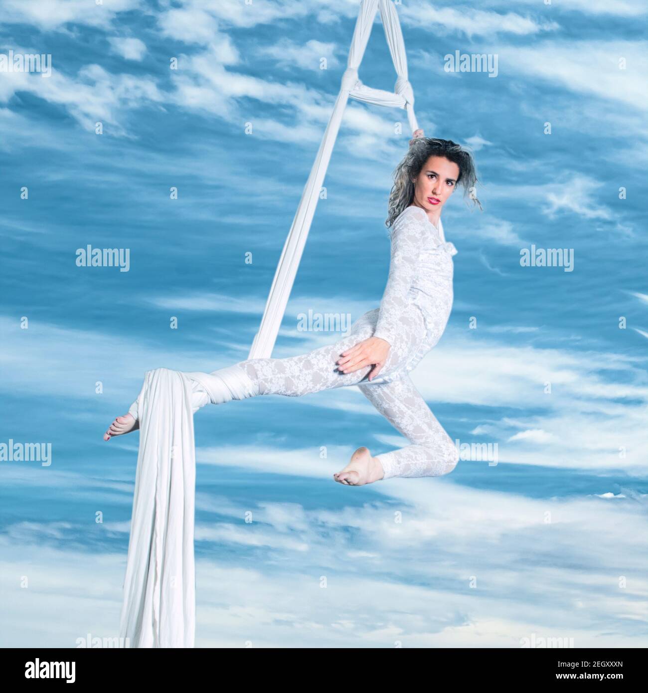 Female Aerialist acrobat performs in the air on fabric with a blue sky ...
