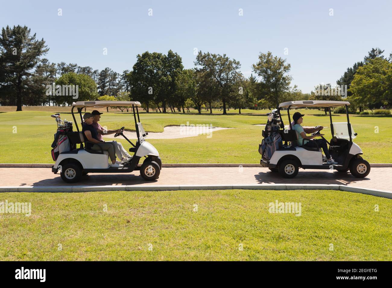 Two caucasian senior couples driving golf buggy on golf course talking ...