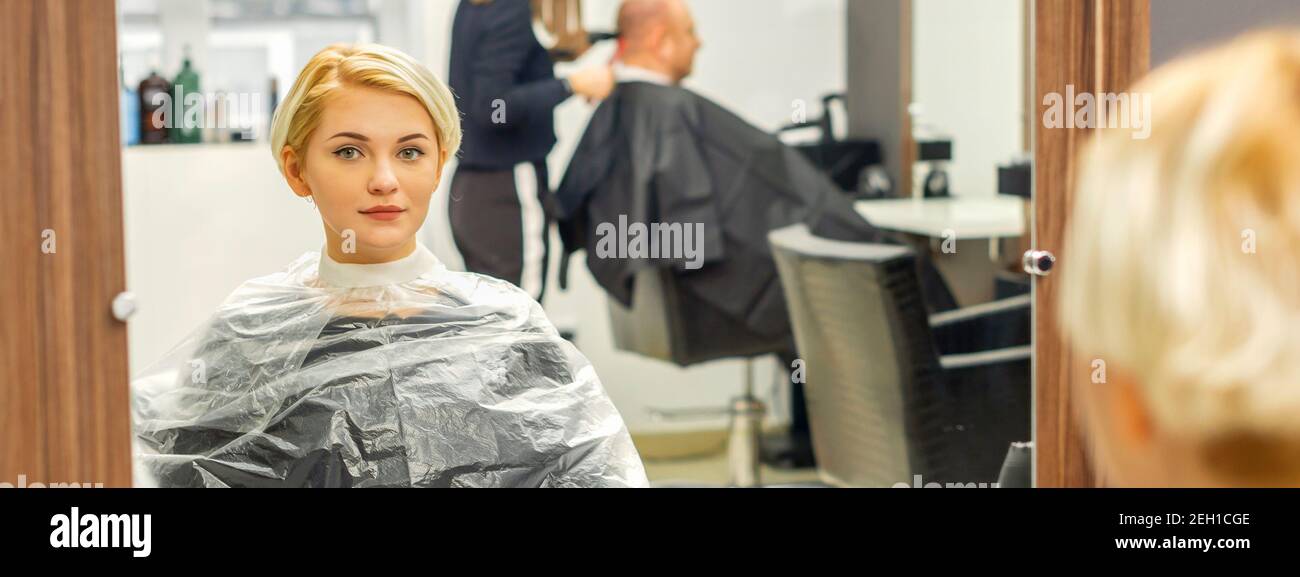 Young female client waiting for the hairdresser looking in the mirror ...