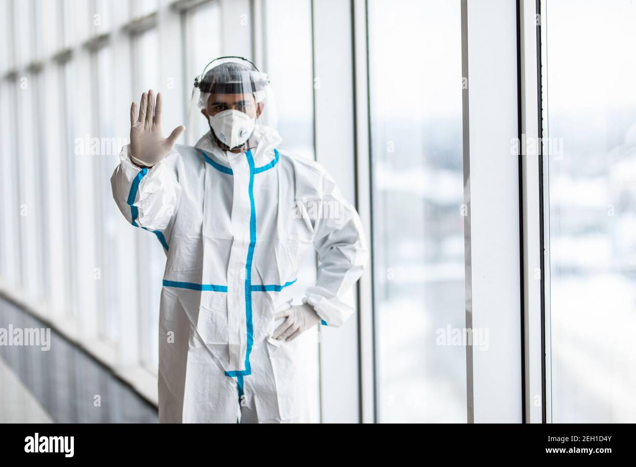 Medic man in a white hazmat suit and mask gesturing stop with hand in ...