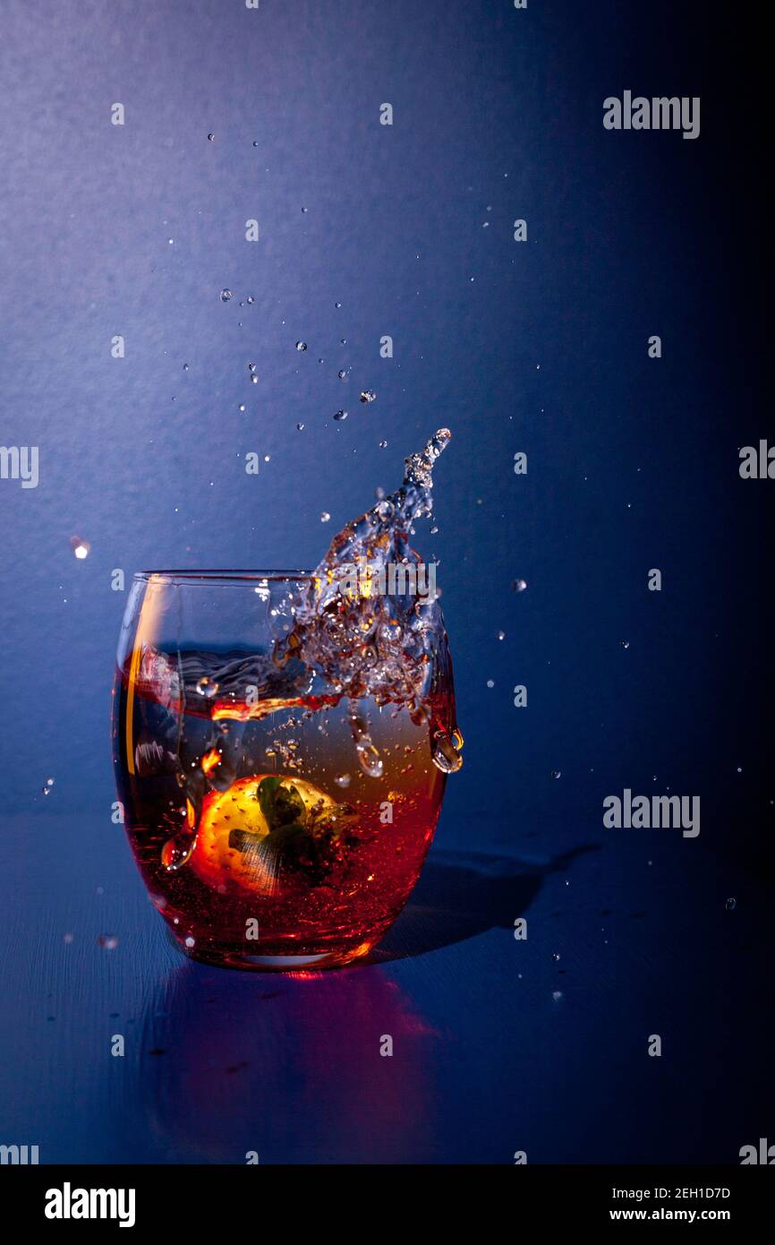 Strawberry dropping into drink on blue backdrop Stock Photo - Alamy