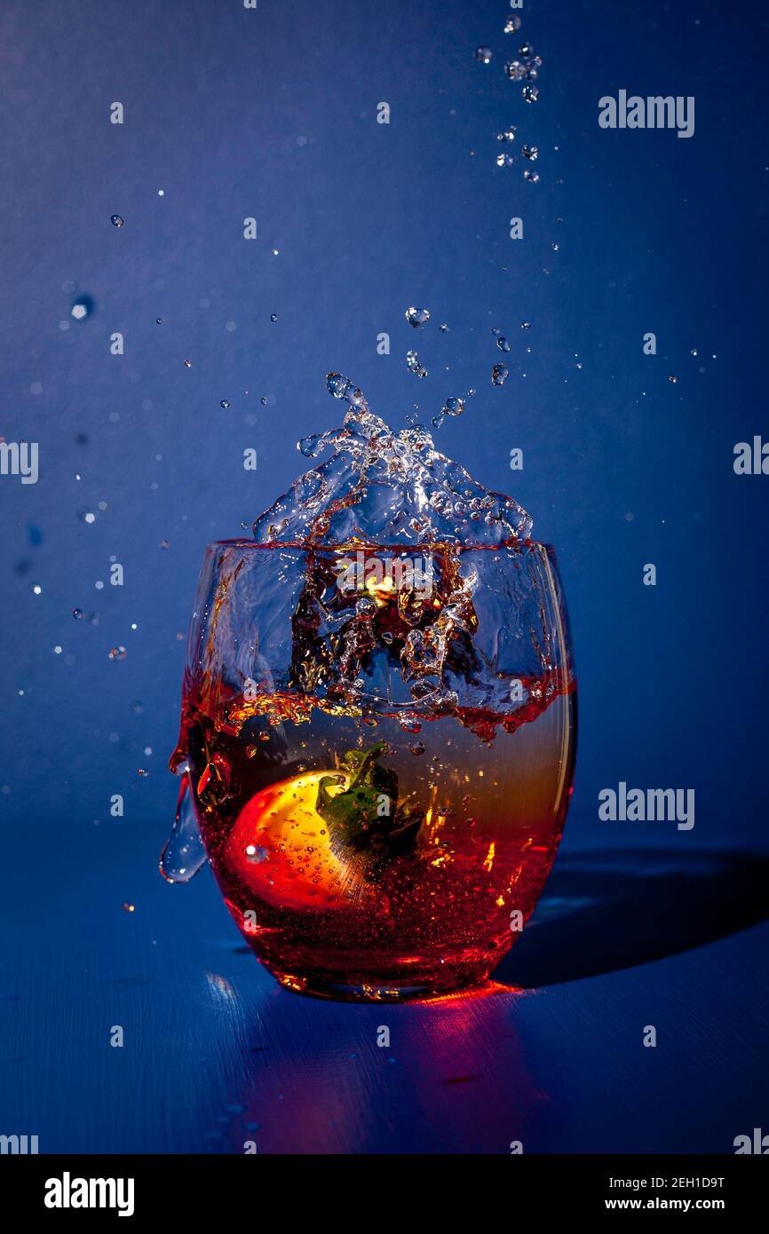 Strawberry dropping into drink on blue backdrop Stock Photo - Alamy