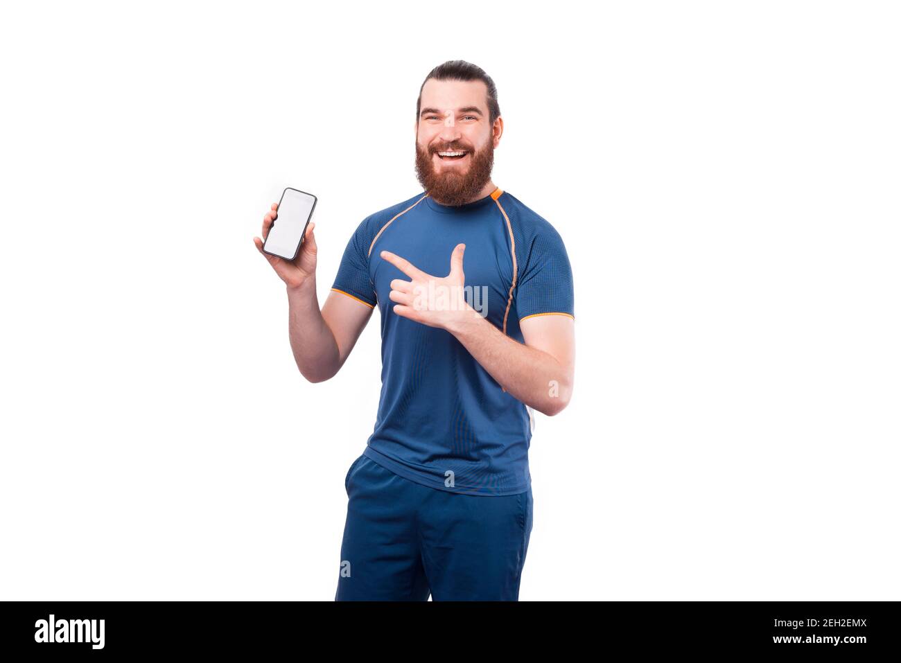 Charming young bearded fitness man pointing at smartphone over white ...