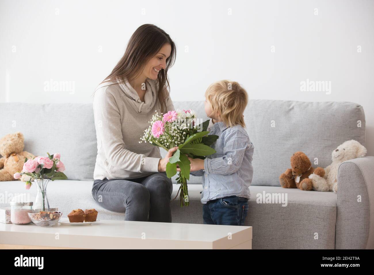 Beautiful blond boy, giving mother flowers and box with little gift for ...