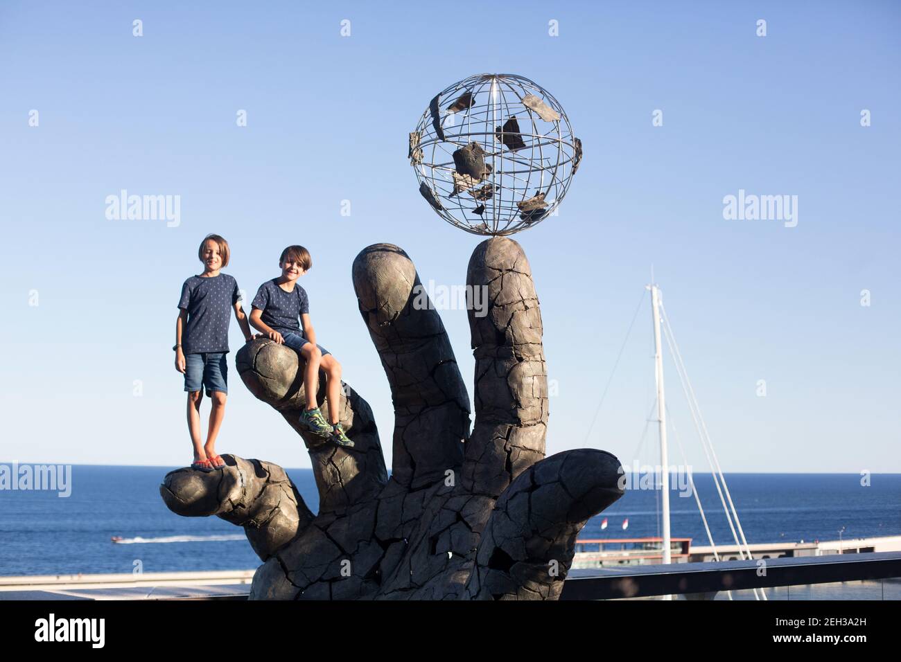 Two children, standing on a art statue of a hand with globe in the ...