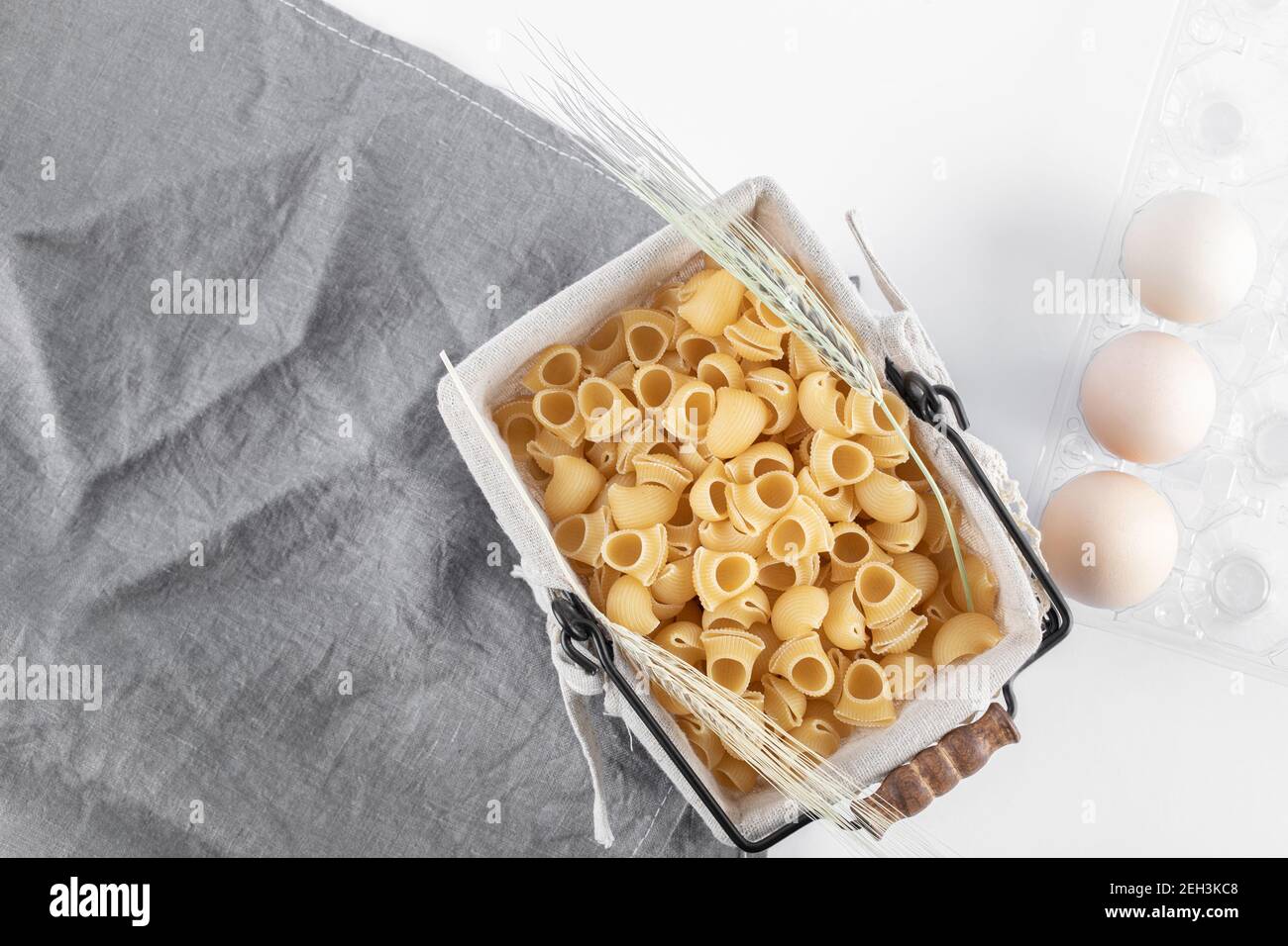 Basket of dry pasta and eggs in container on white surface Stock Photo ...