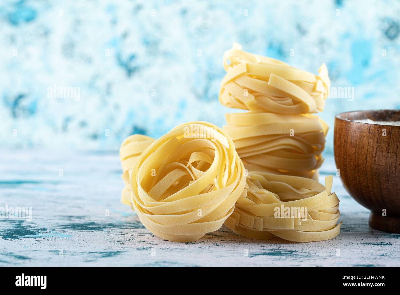 Dry tagliatelle nests and bowl of flour on colorful surface Stock Photo ...