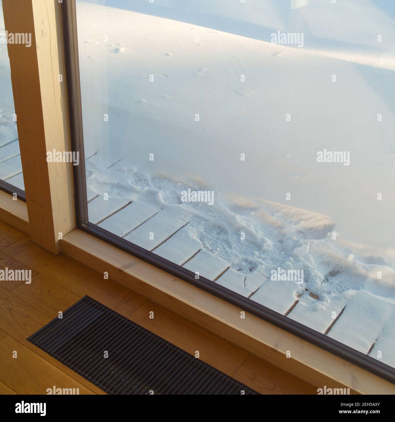 A heater grill on a harfwood floor and footprints on the snow behind a ...