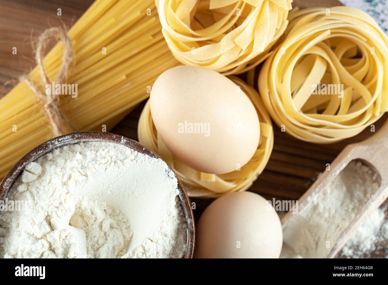 Two types raw pasta with eggs and bowl of flour on wooden board Stock ...