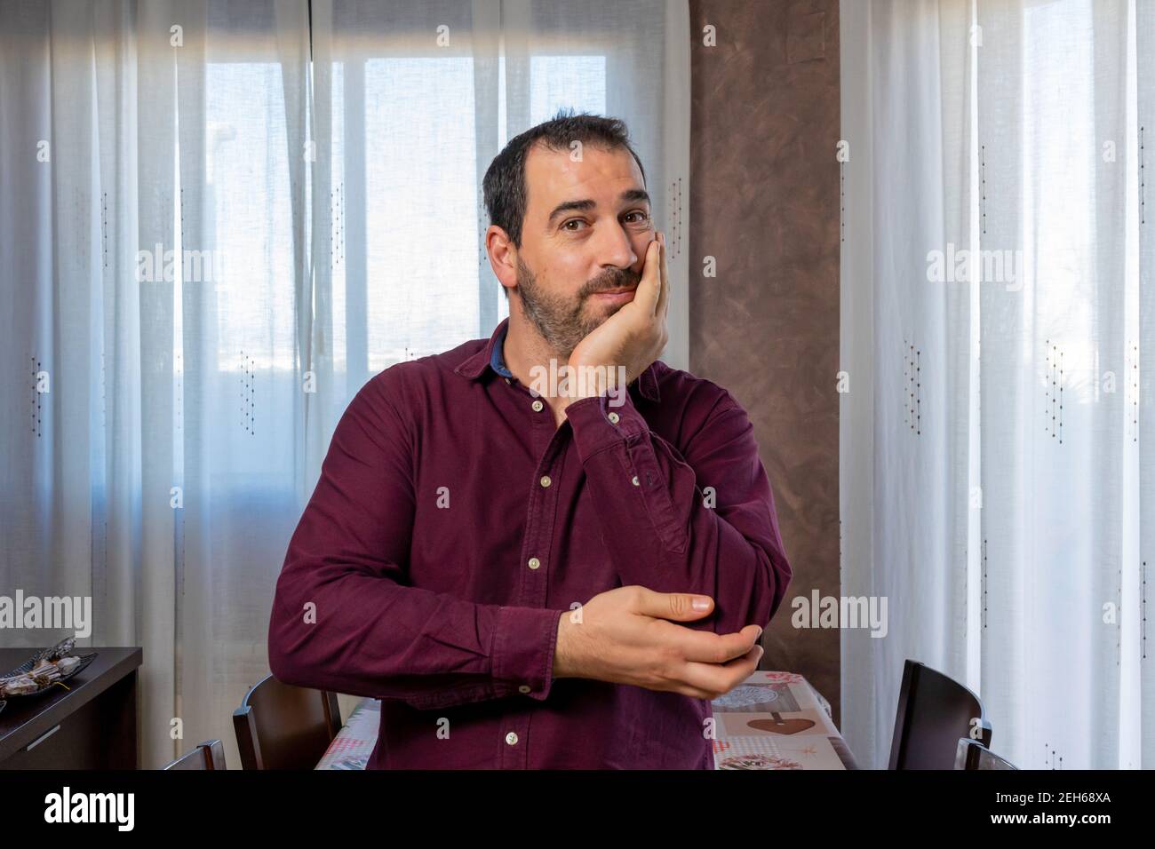 Bearded man in a purple shirt leaning his face on his hand with ...