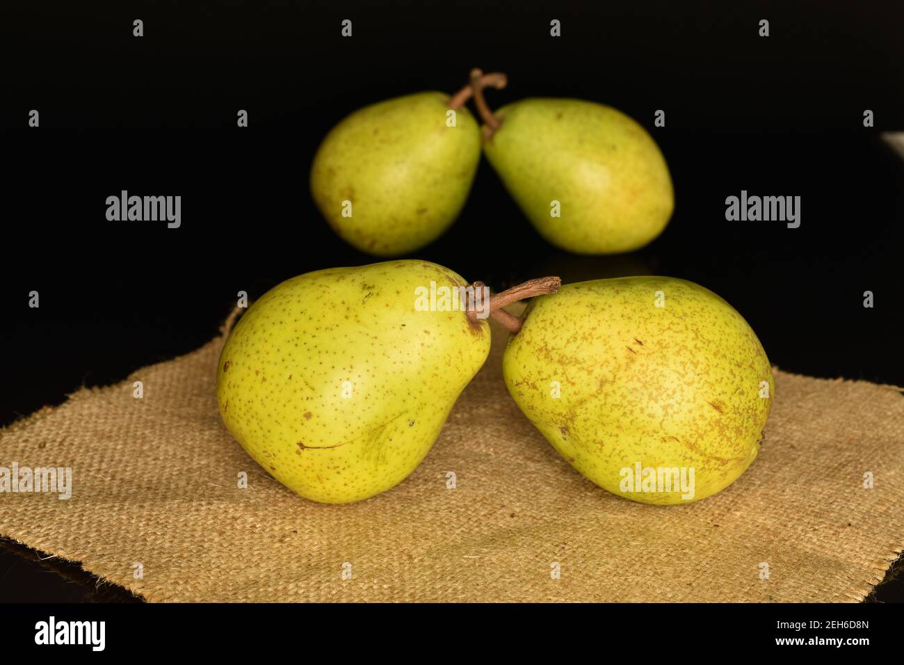 Four whole ripe juicy tasty Lucas pears lie on jute fabric, on a black ...