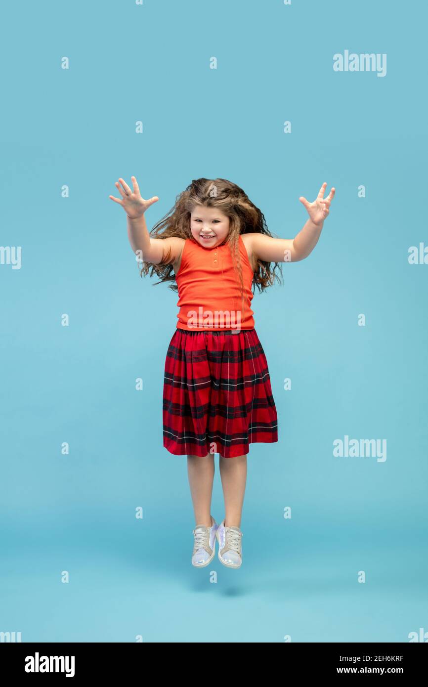 Jumping high. Happy, smiley little caucasian girl isolated on blue ...