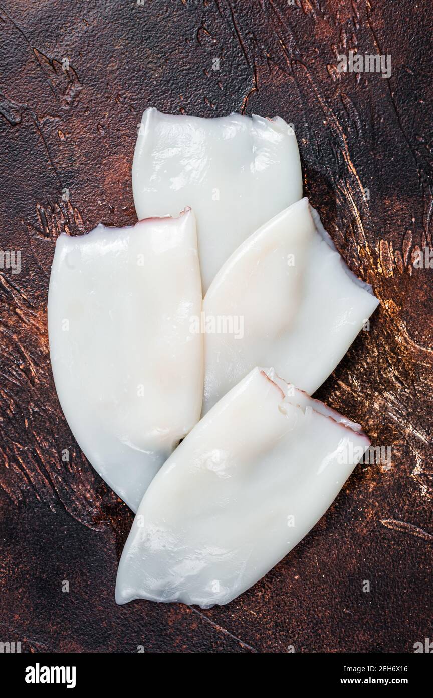 Raw Squid or Calamari tubes on a kitchen table. Dark background. Top ...