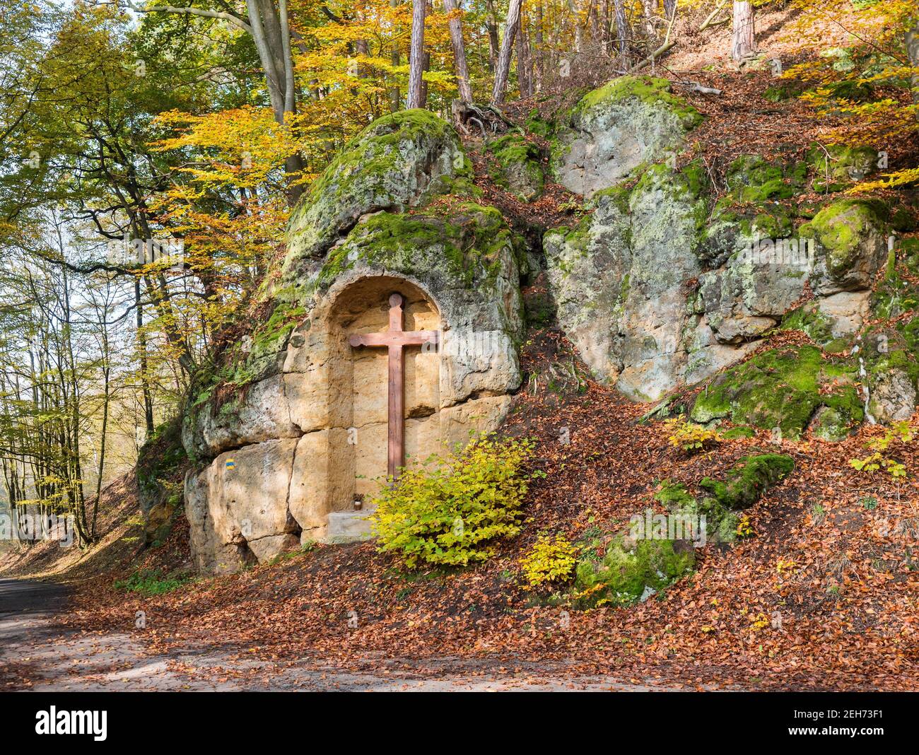 Wooden cross at sandstone rock niche along country road at colorful ...