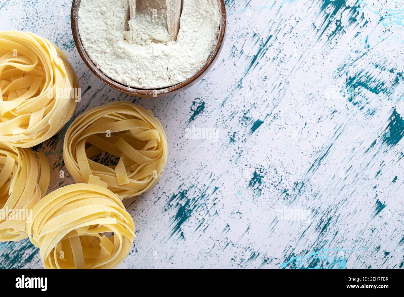 Dry tagliatelle nests and bowl of flour on colorful surface Stock Photo ...