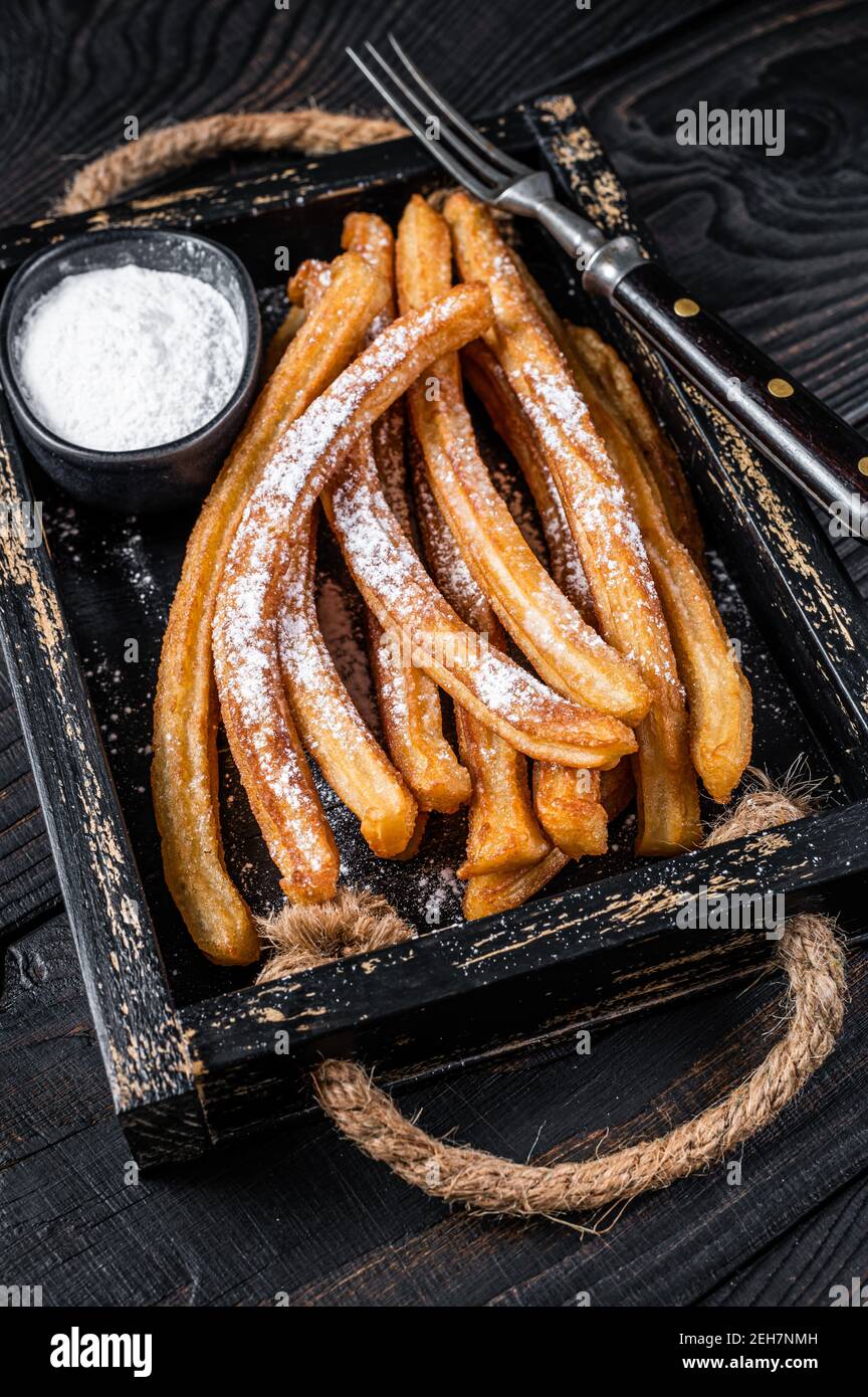 Churros fried sticks with sugar powder in wooden tray. Black background ...