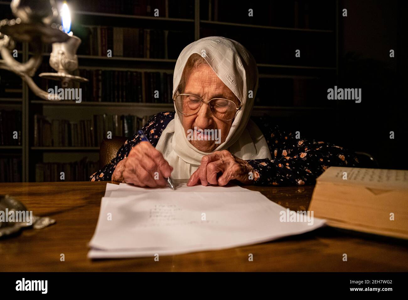 Old lady reading books in dark room with candles light and writing down ...